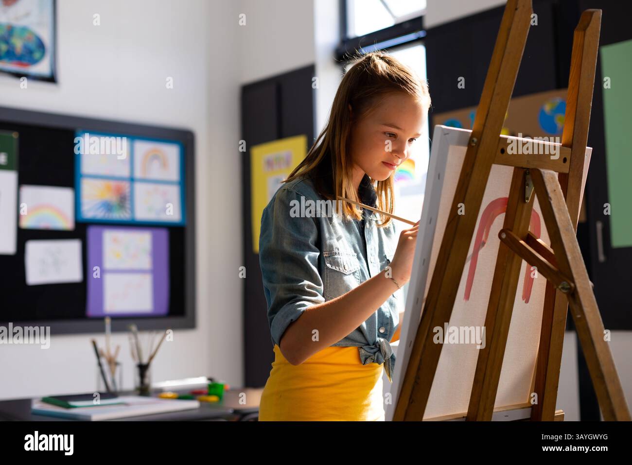 Female child painting on white canvas at wooden easel in art classroom ...