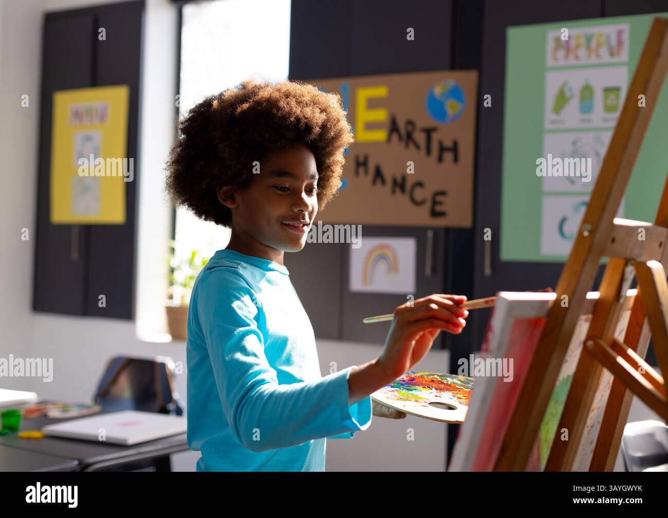 Child boy painting on easel in art classroom with paintbrush, palette ...