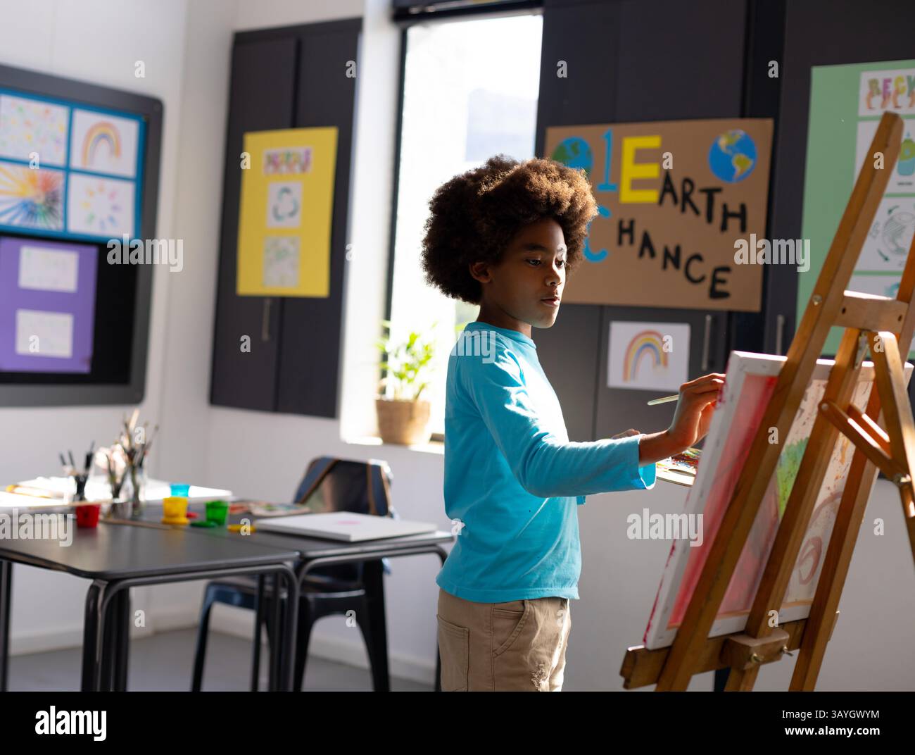 Boy child painting on wooden easel in school art classroom with ...