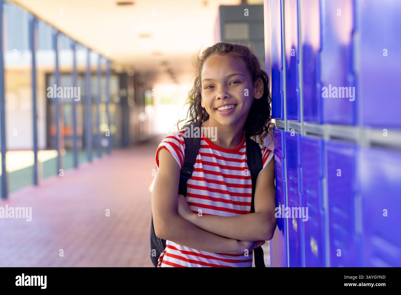 Multiracial girl leaning against blue lockers in school corridor ...