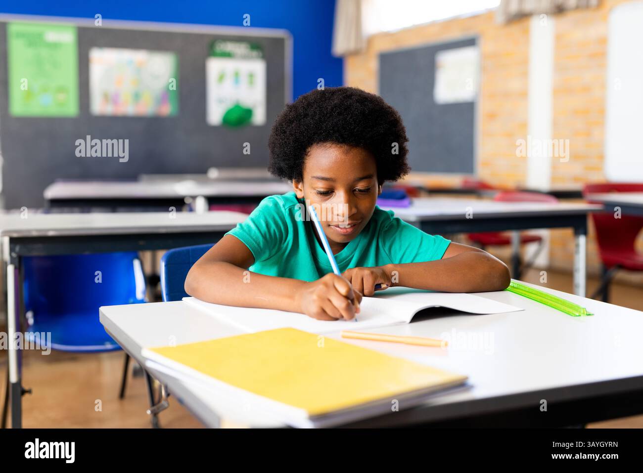 Boy writing in open notebook at school classroom desk, with pencil ...