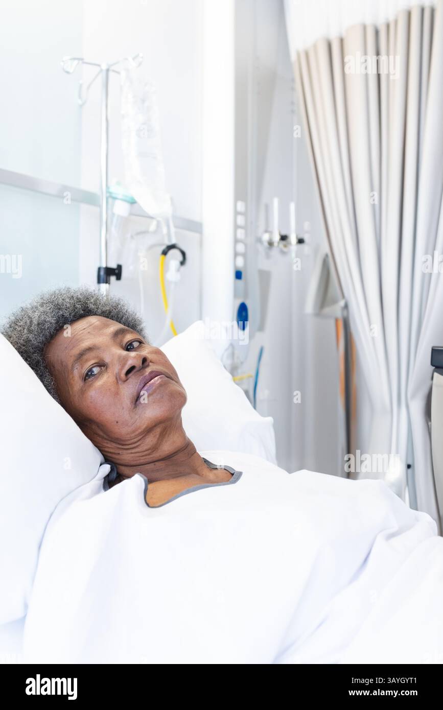 Senior African American woman lying in hospital room on bed, with IV drip and infusion machine ...