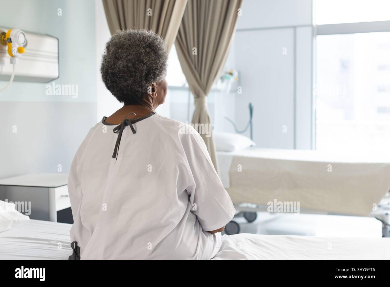 African American senior woman sitting on bed facing window in hospital ...