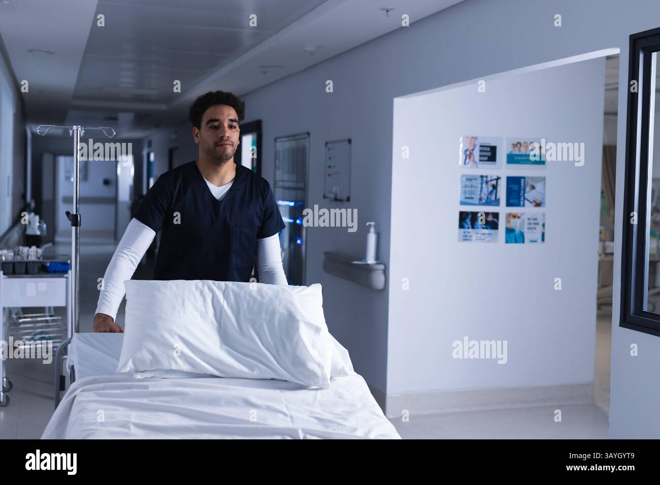 Young man pushing empty hospital bed down bright hospital corridor ...