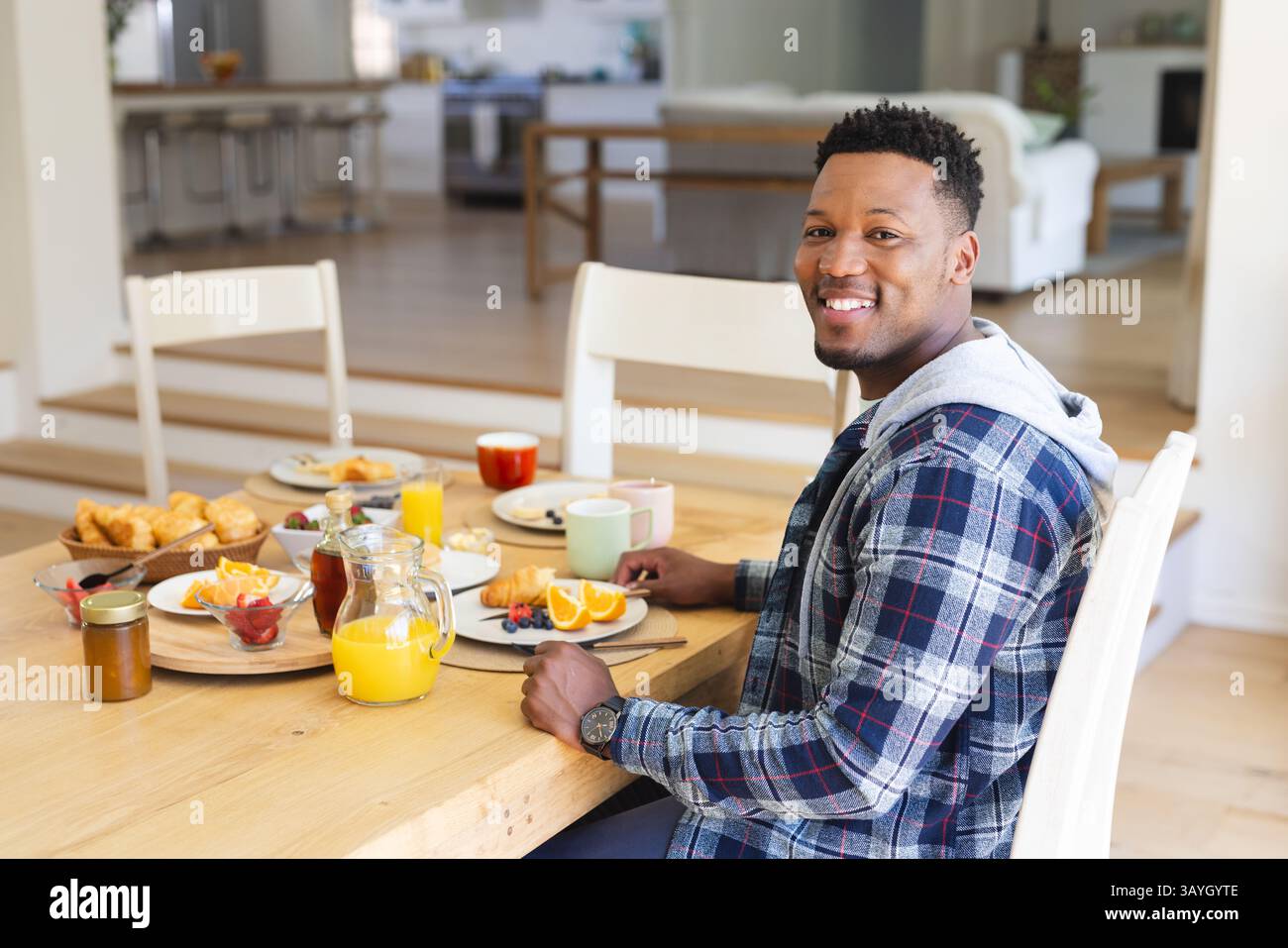 African American man eating breakfast croissants at dining table in ...