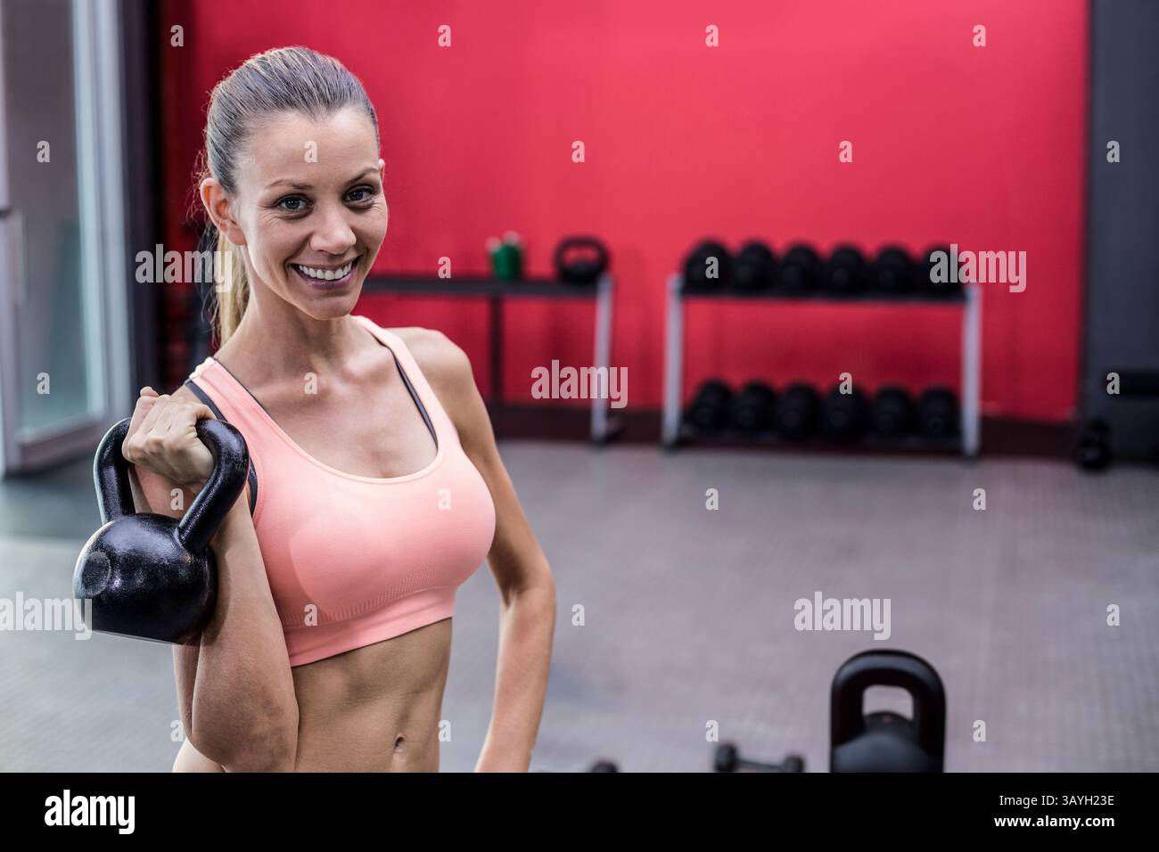 Mid-adult woman lifting kettlebell in modern gym weight-training area ...