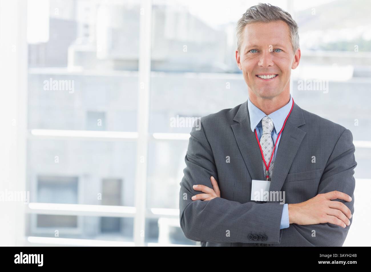 Young adult Indian man crossing arms in office by windows, with badge ...