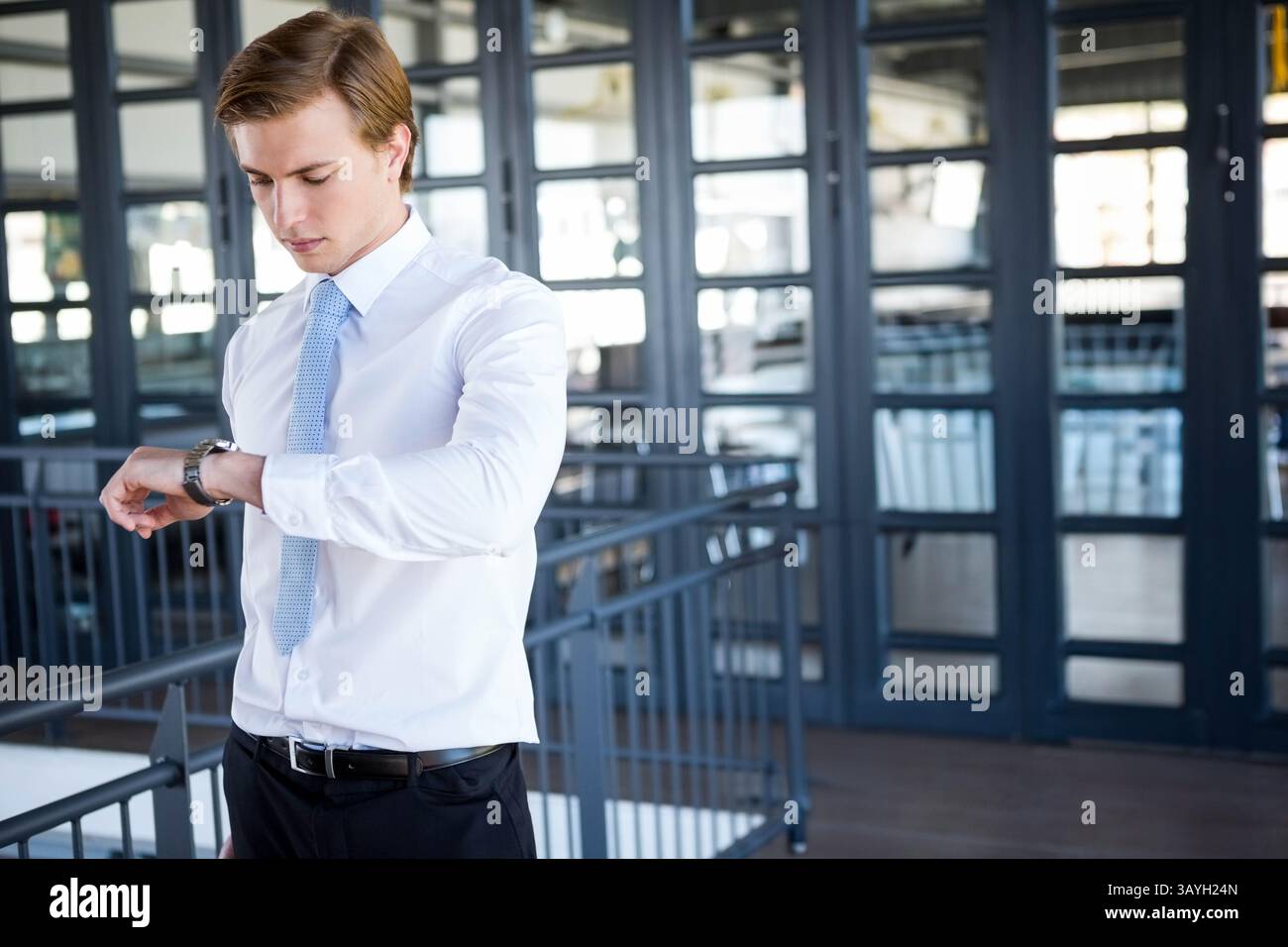 Businessman checking analog wristwatch in office lobby by glass walls ...