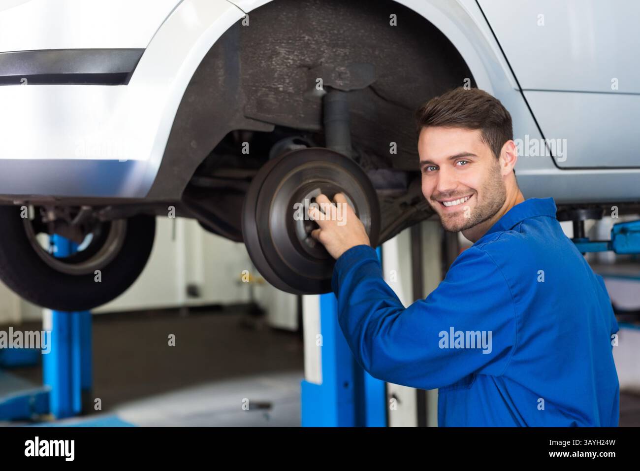 Male mechanic inspecting brake drum under car in repair garage, with ...