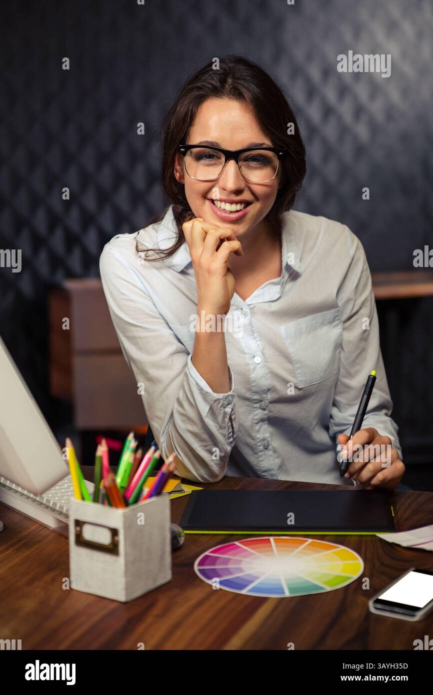 Woman sitting at desk in modern studio, holding stylus over graphics ...