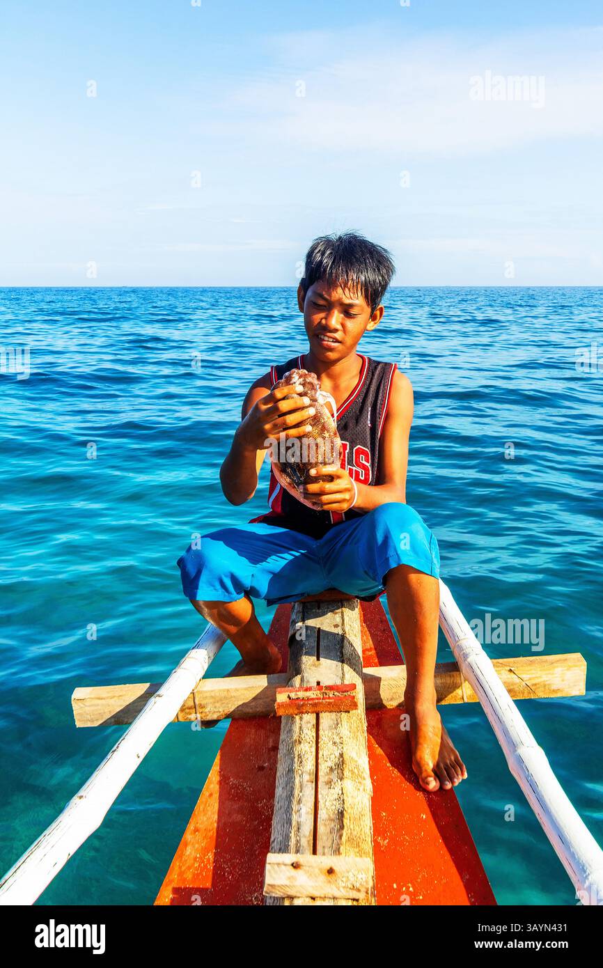 A Filipino boy holds a freshly caught cuttlefish while sitting on a ...