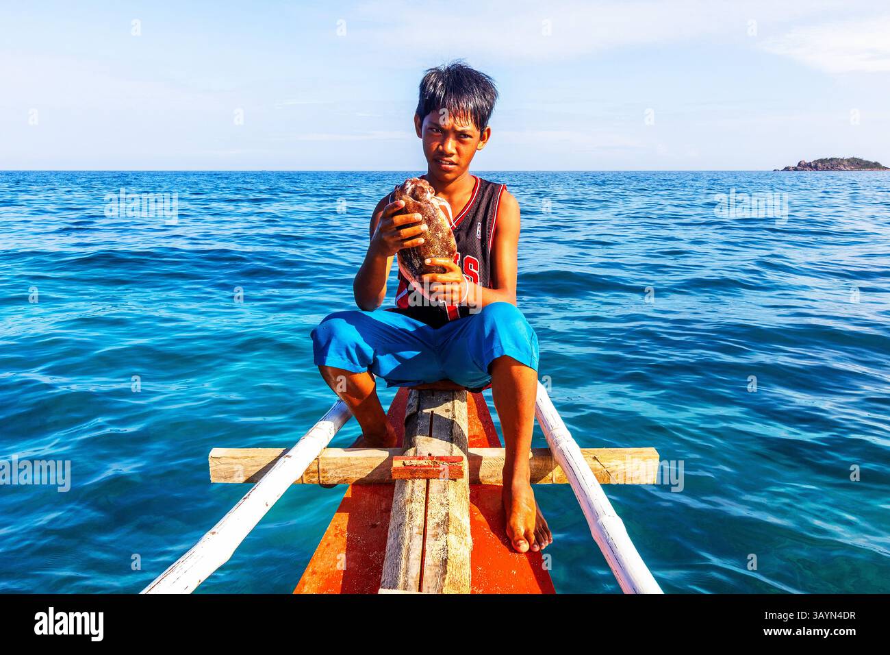 A Filipino boy holds a freshly caught cuttlefish while sitting on a ...