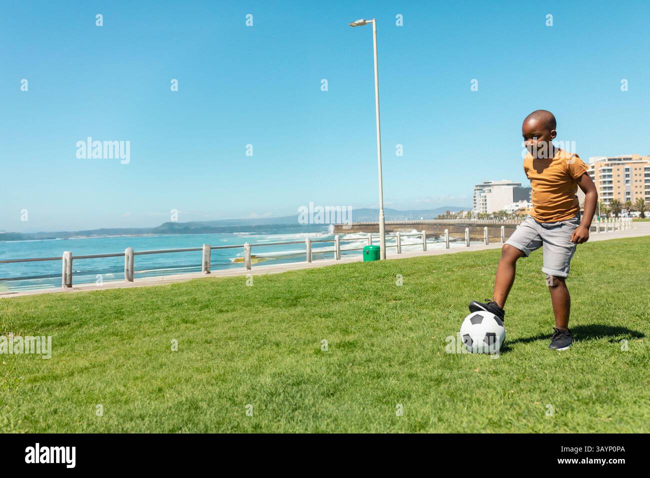 African American boy balancing soccer ball on grass beside ocean ...
