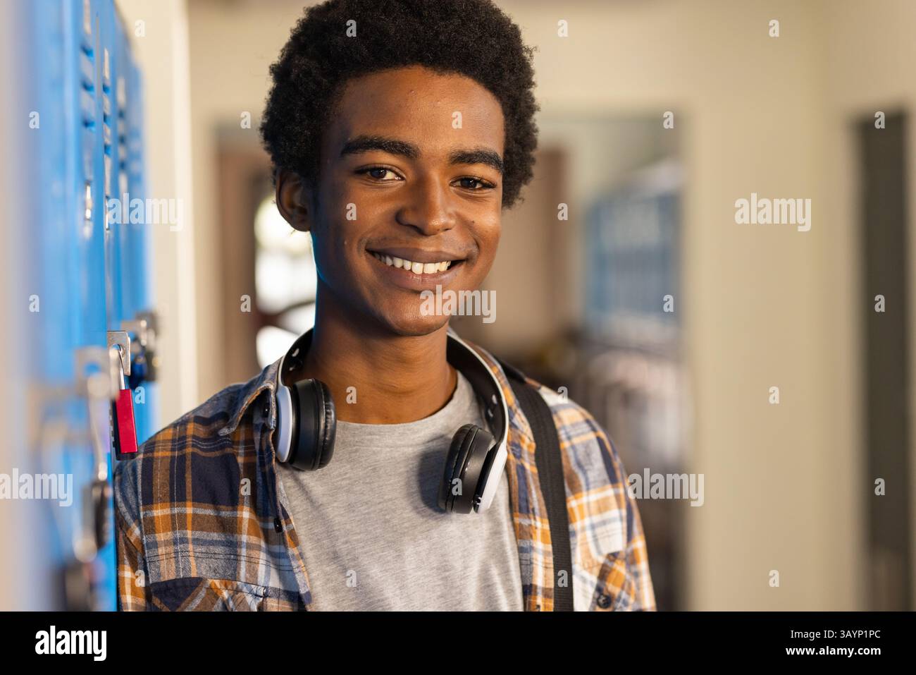 African American teenage student leaning against blue lockers in school ...