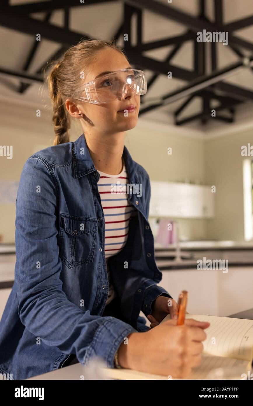 Young adult woman sitting at school lab bench writing in notebook with ...