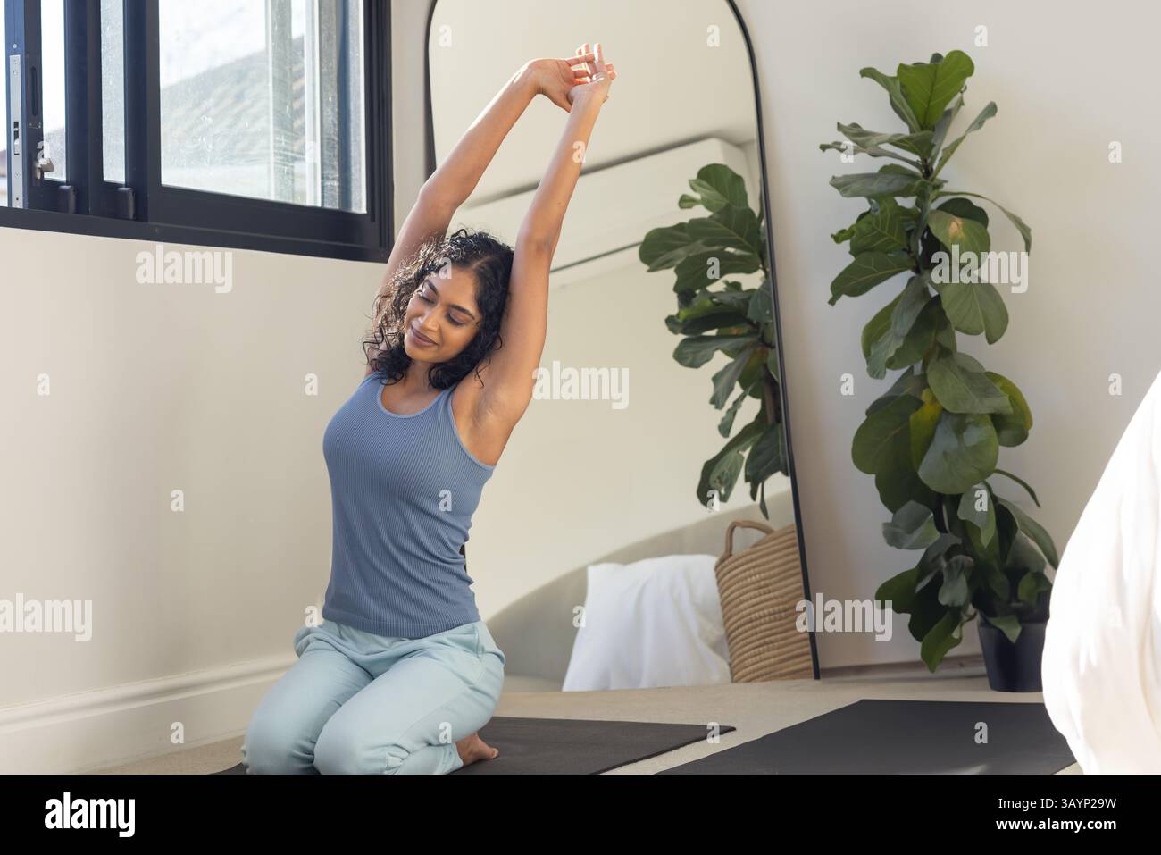 Indian woman in 20s kneeling stretching overhead on yoga mat near ...