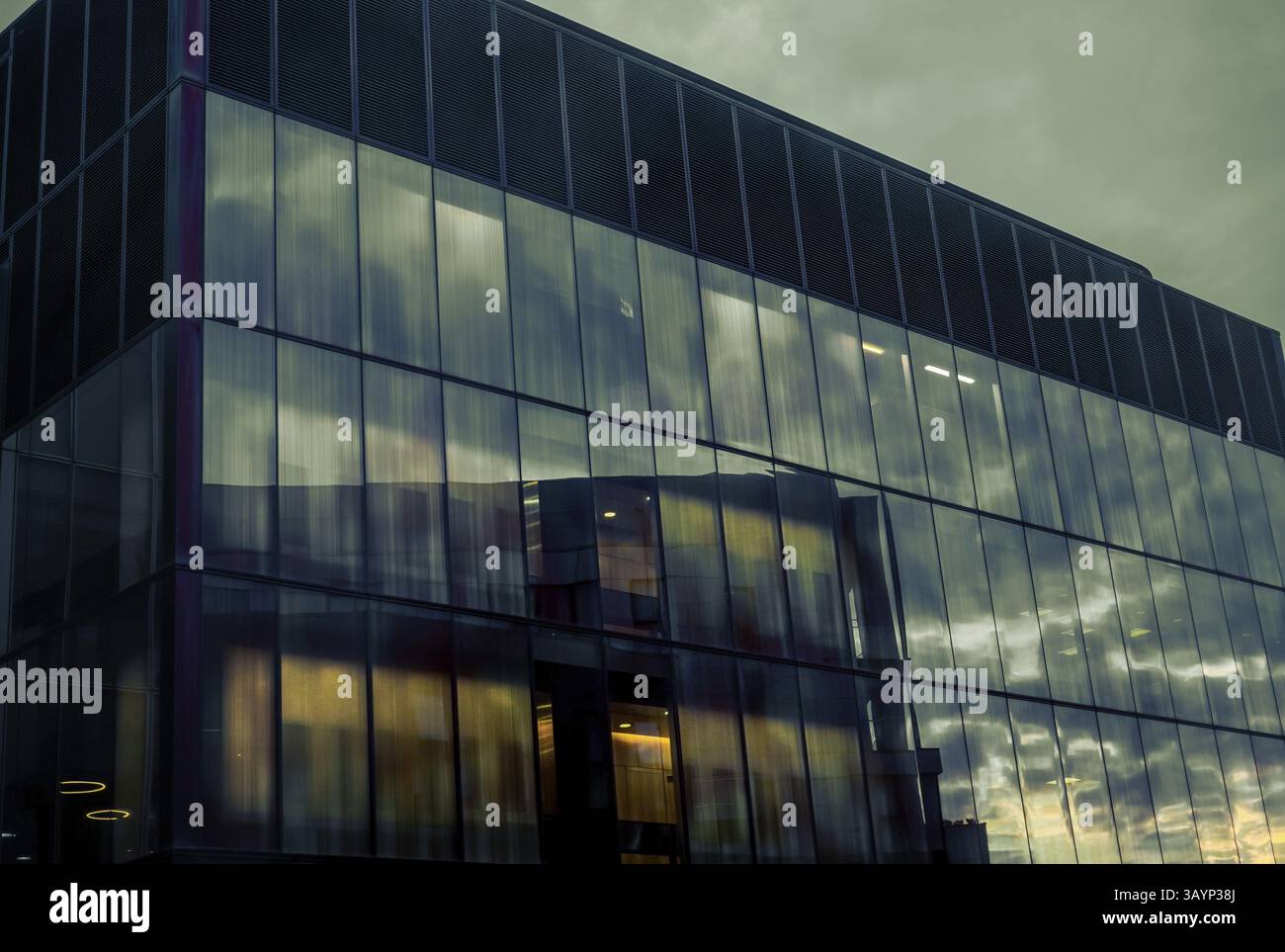 Building with dark glass facade reflects clouds in the evening ...