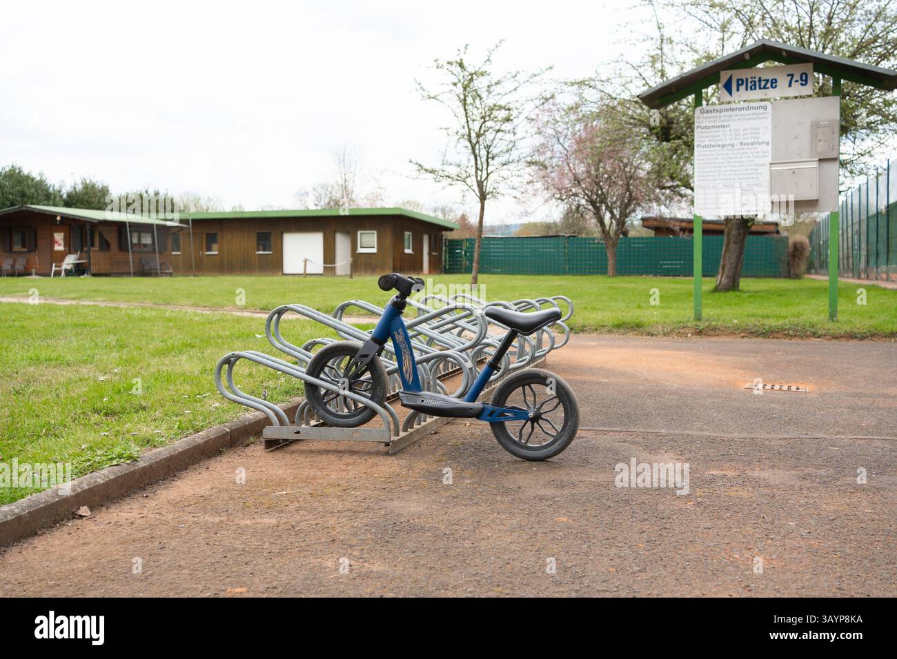 A blue balance bike parked in a metal bike rack at a rural park. The ...
