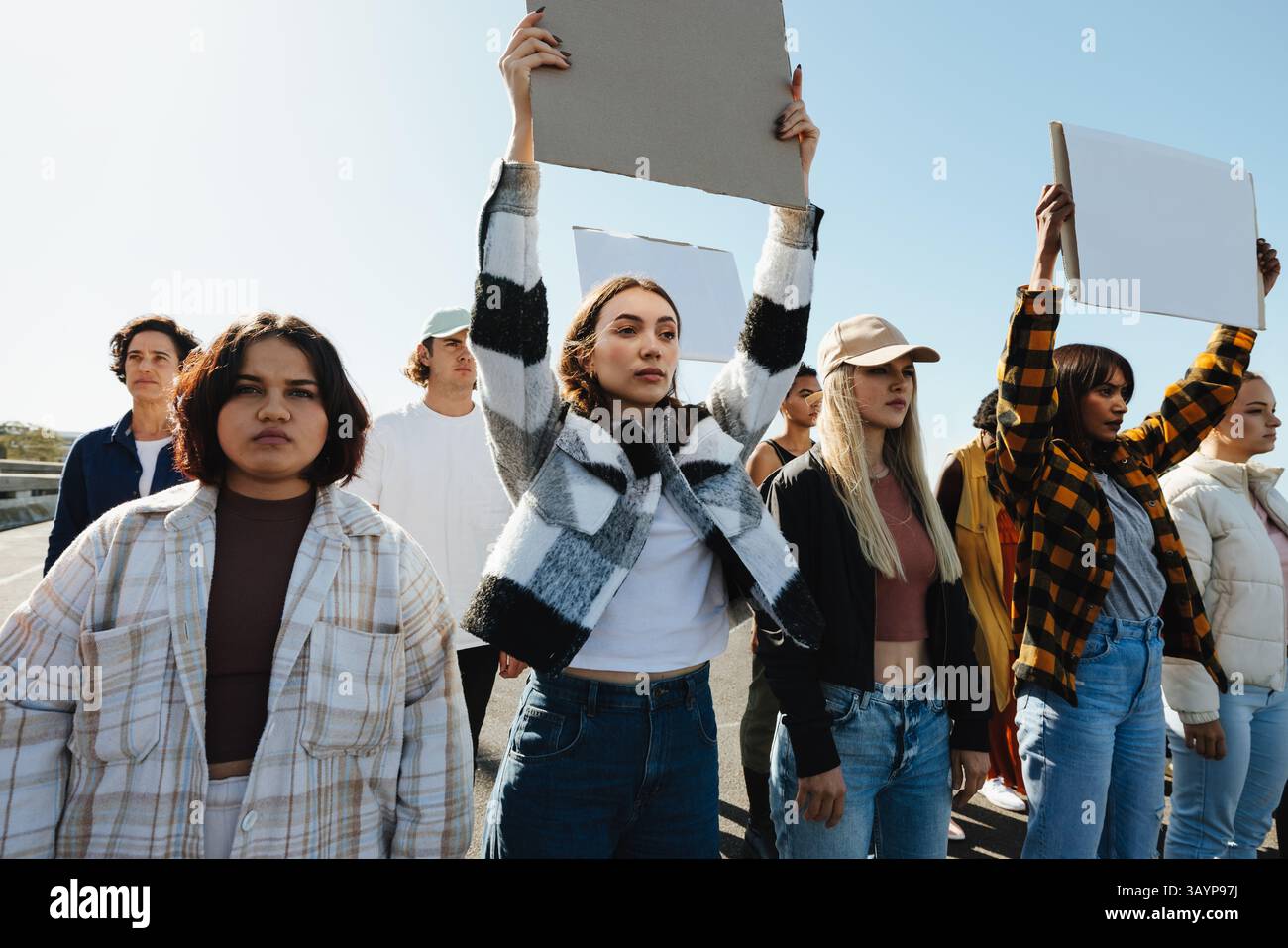 A diverse group of people gathered outdoors, holding signs ...
