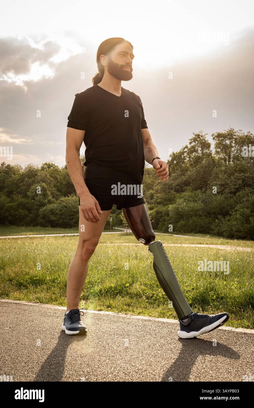 Confident athlete with prosthetic leg walking outdoors at sunset ...