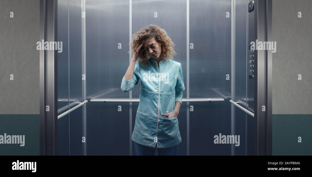 Stressed tired female doctor standing in the elevator and touching her ...