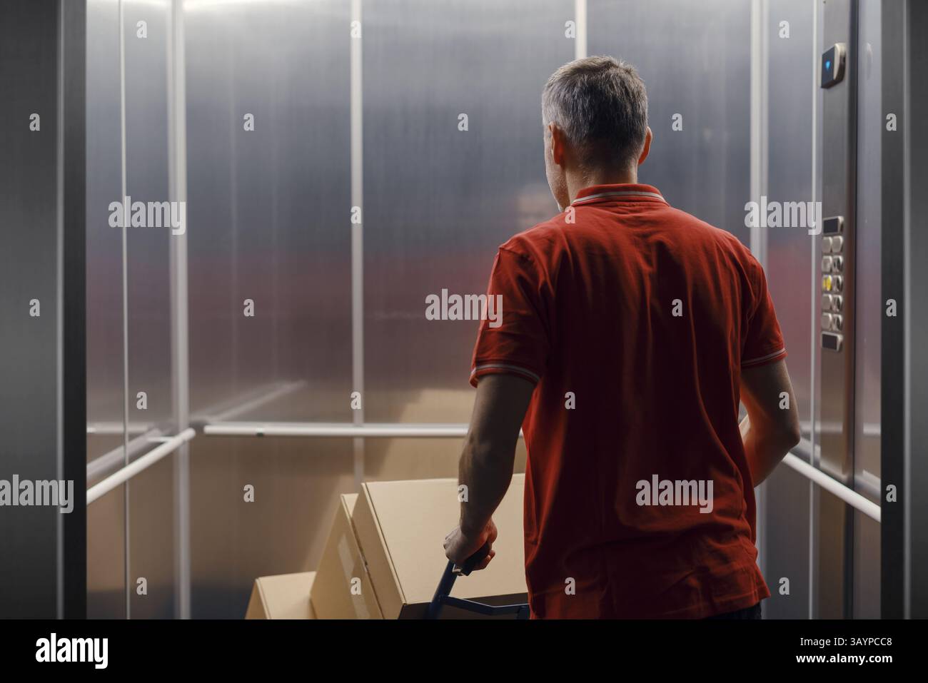 Delivery man getting in the elevator and pushing a hand truck loaded ...