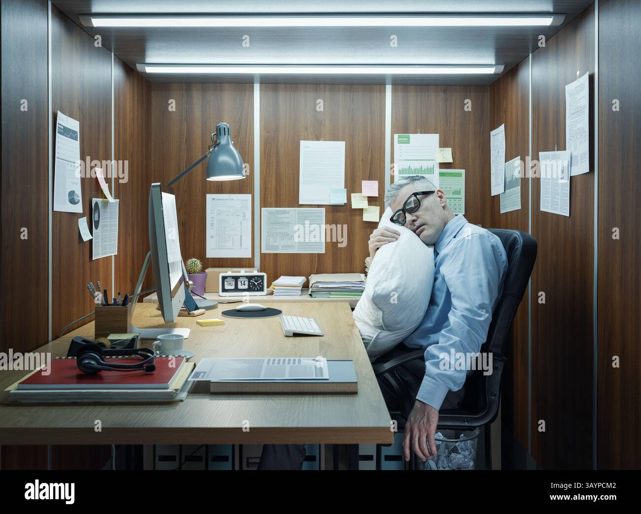 Tired corporate business employee sleeping at his desk in a tiny office ...
