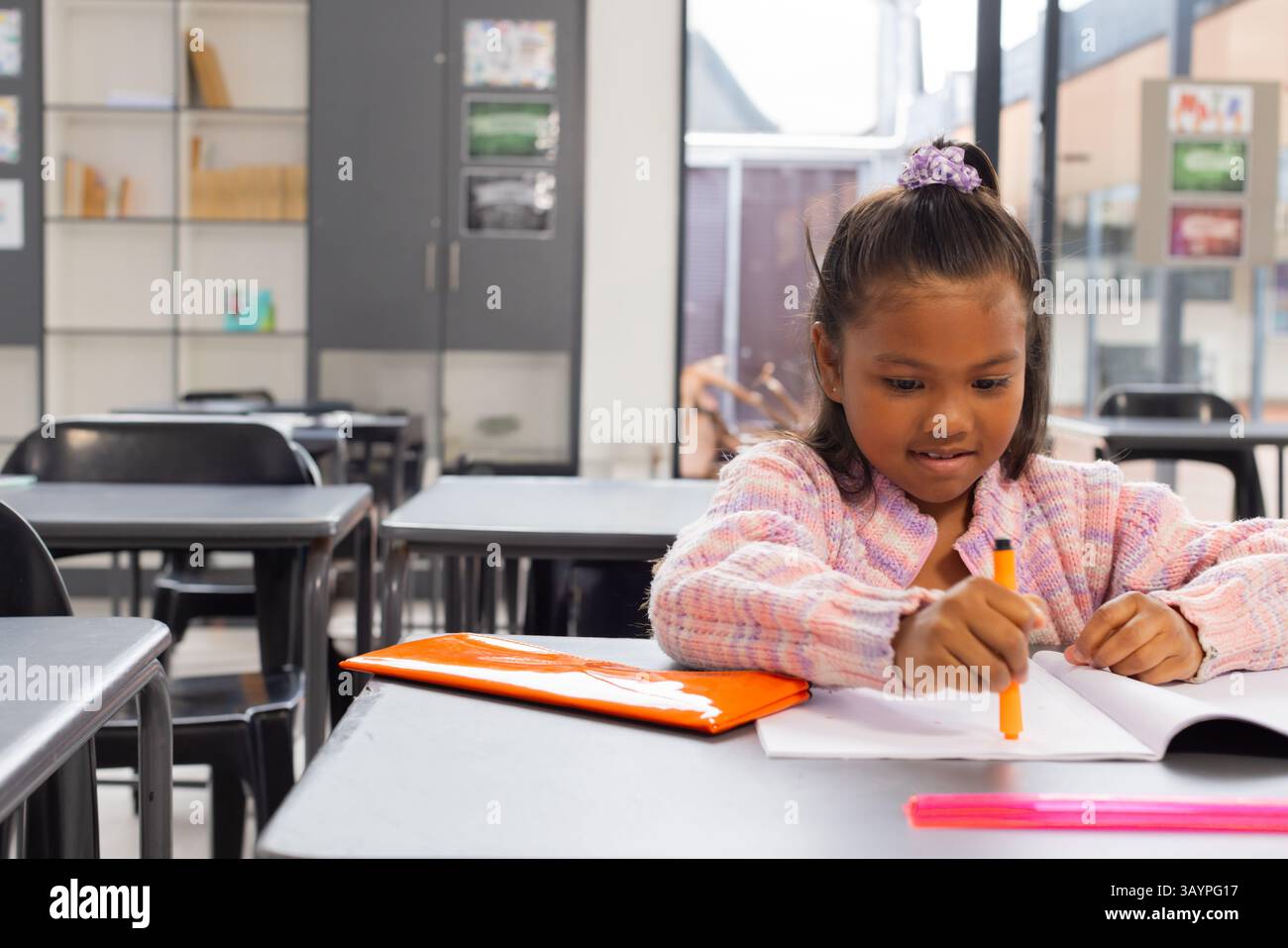 Girl child writing in notebook in elementary classroom, using orange ...