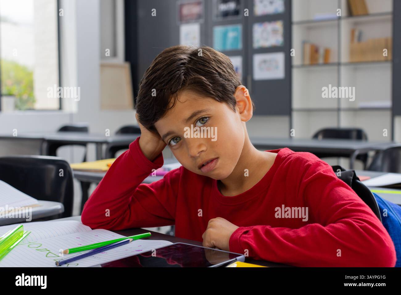 Boy resting head on hand at student desk in classroom, with open ...