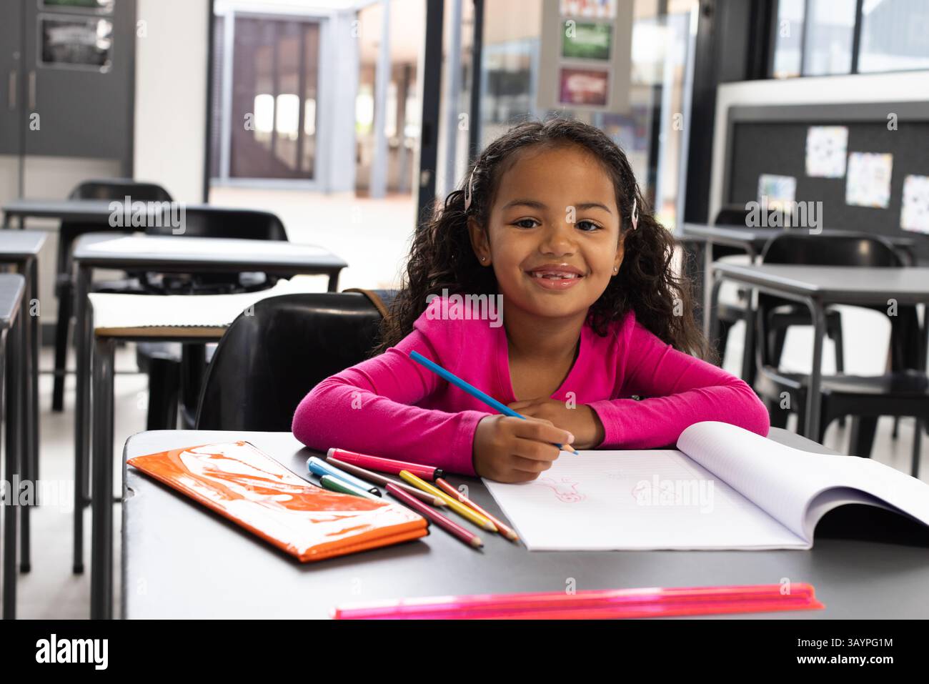 Girl drawing on white paper at modern classroom desk, using colored ...