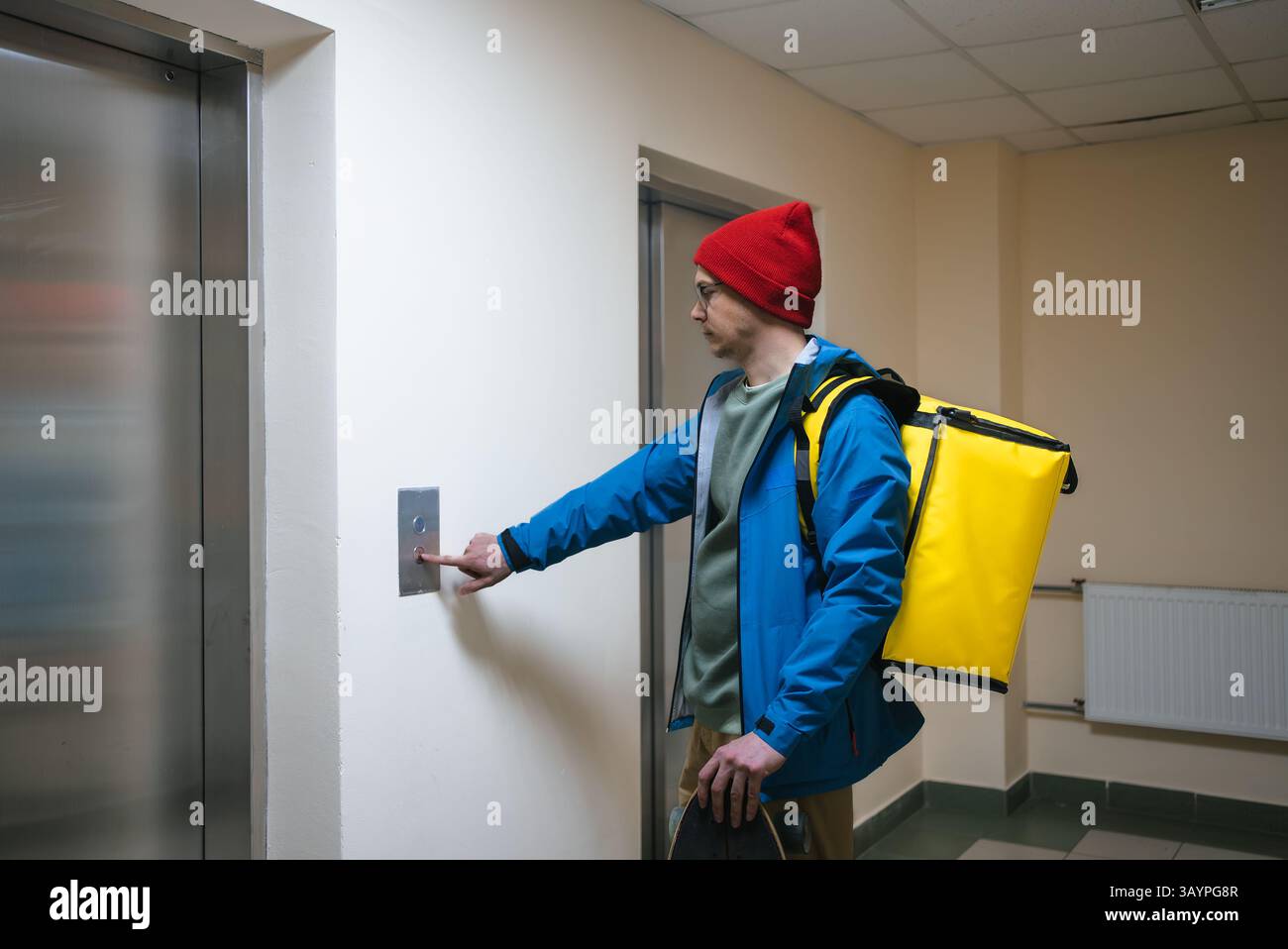 Courier pushing elevator button in building corridor while delivering ...