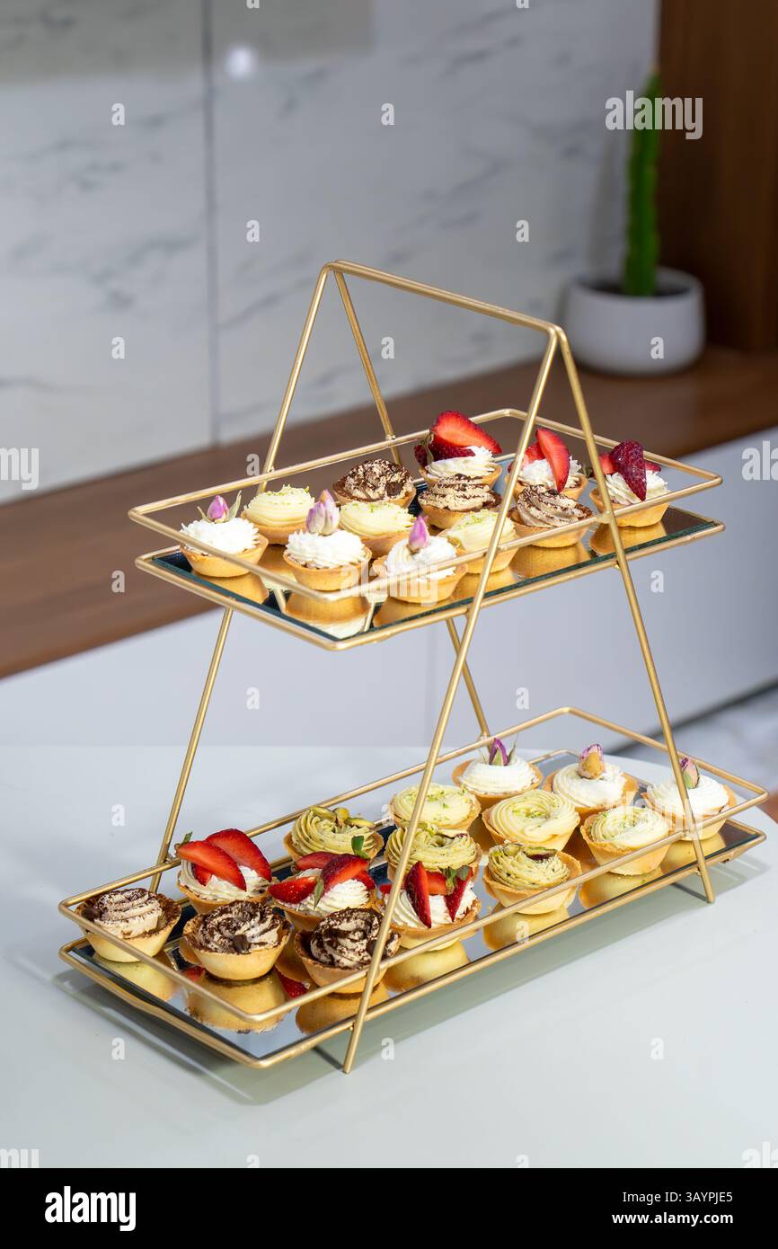 Elegant two-tier dessert stand with assorted mini tarts topped with fresh strawberries, whipped ...
