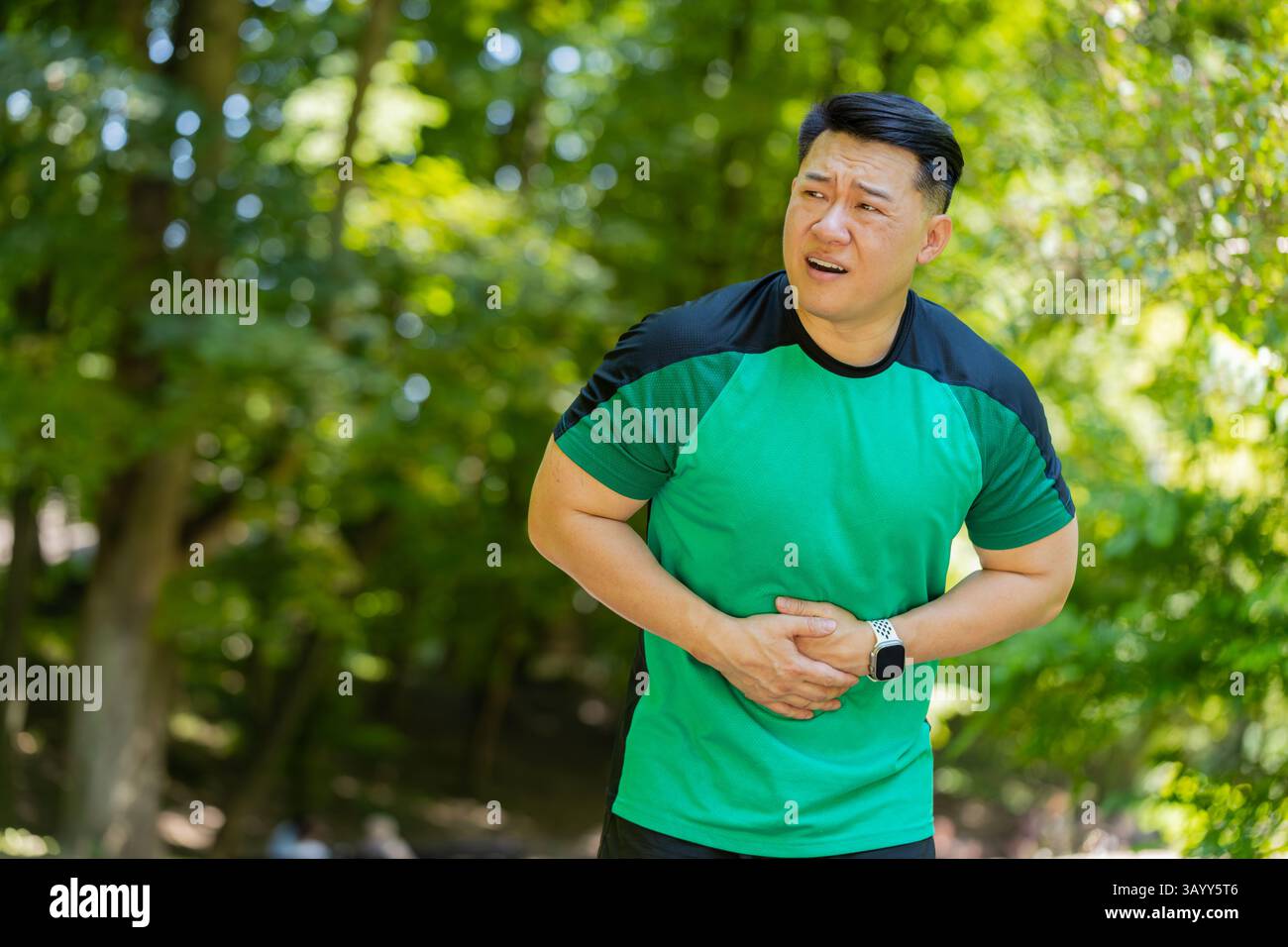 Middle-aged Asian runner feeling sudden strong abdominal stomach ache ...