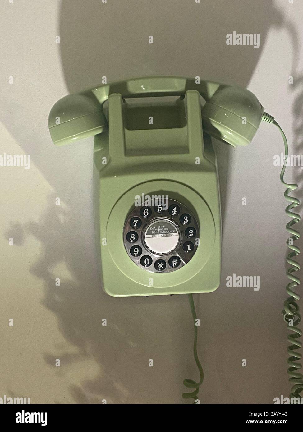 Green vintage rotary phone hanging on a white wall, casting shadows ...