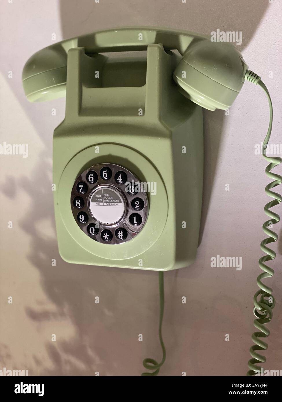 Vintage green rotary telephone hanging on white wall, featuring curled ...