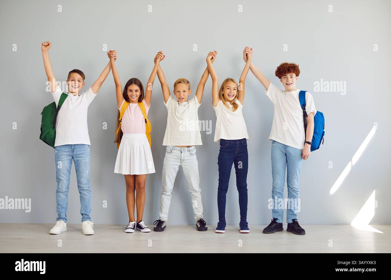 Happy school children standing on gray background holding hands up and ...