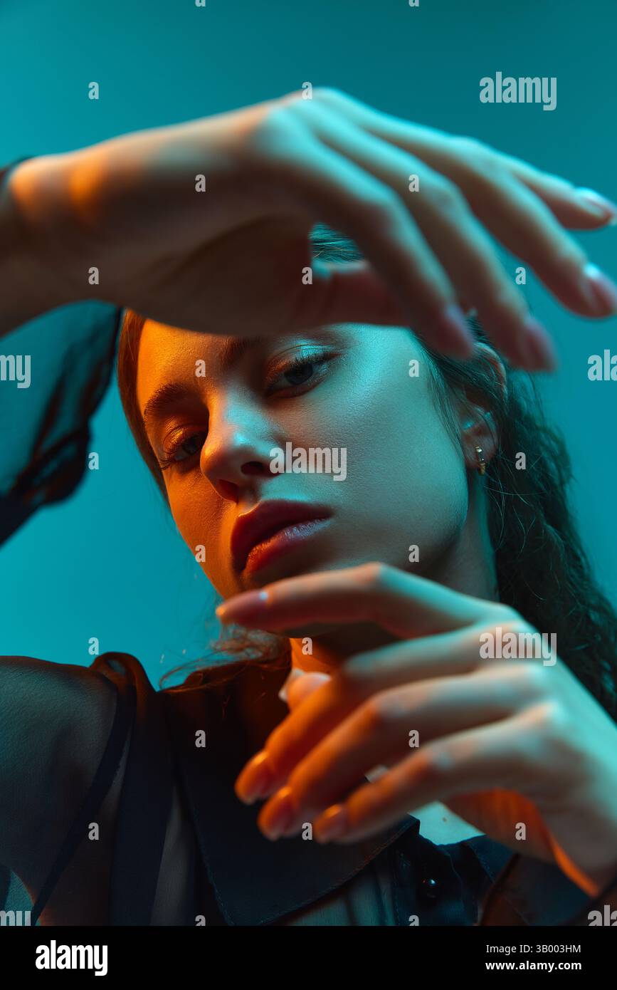 Female portrait framed by soft curved hands under intense teal lighting ...