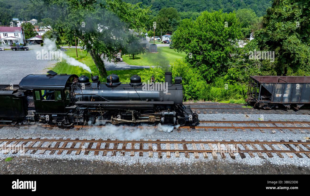 A vintage steam locomotive steams along the tracks in a quaint town ...