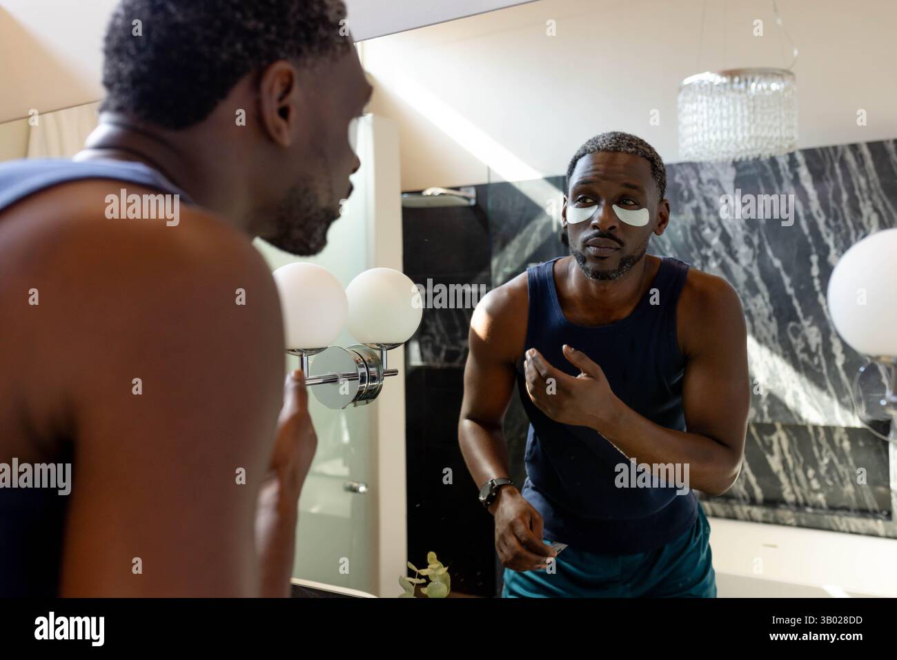 Leaning African American man applying under-eye gel patches at modern ...