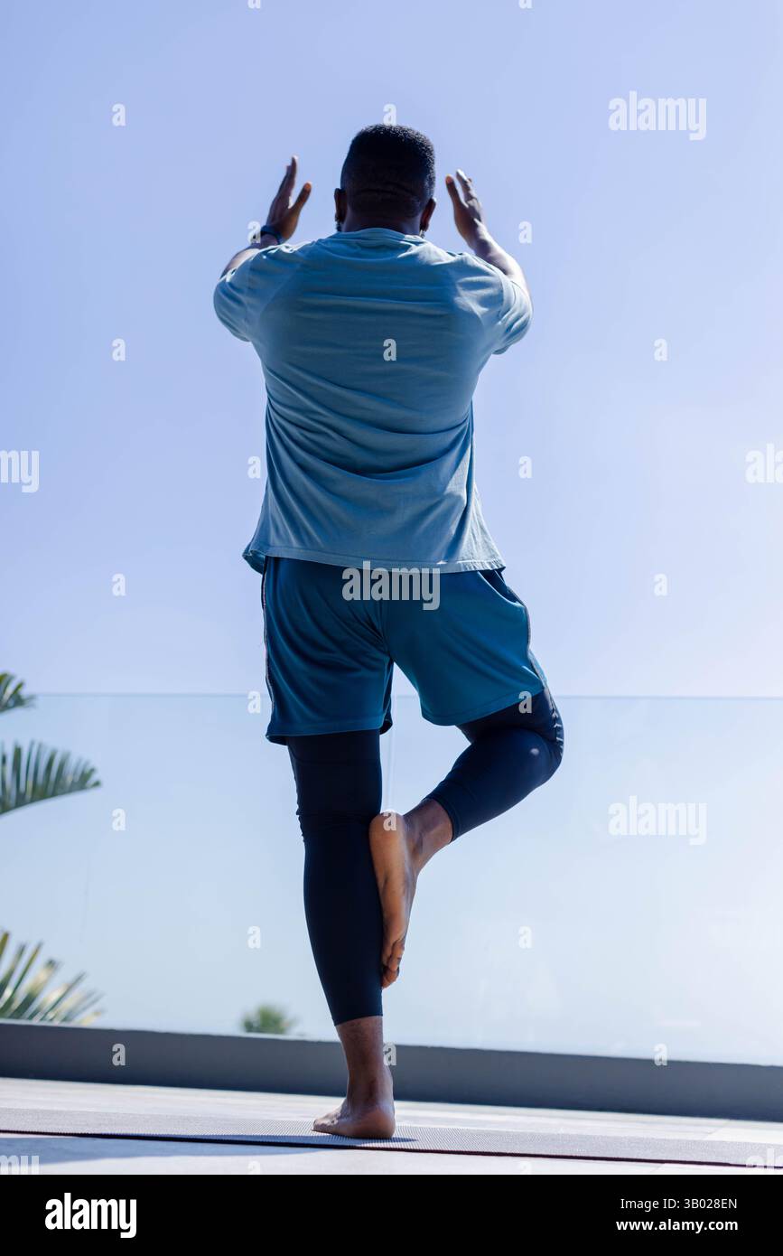 Balancing African American man on outdoor balcony with glass railing ...