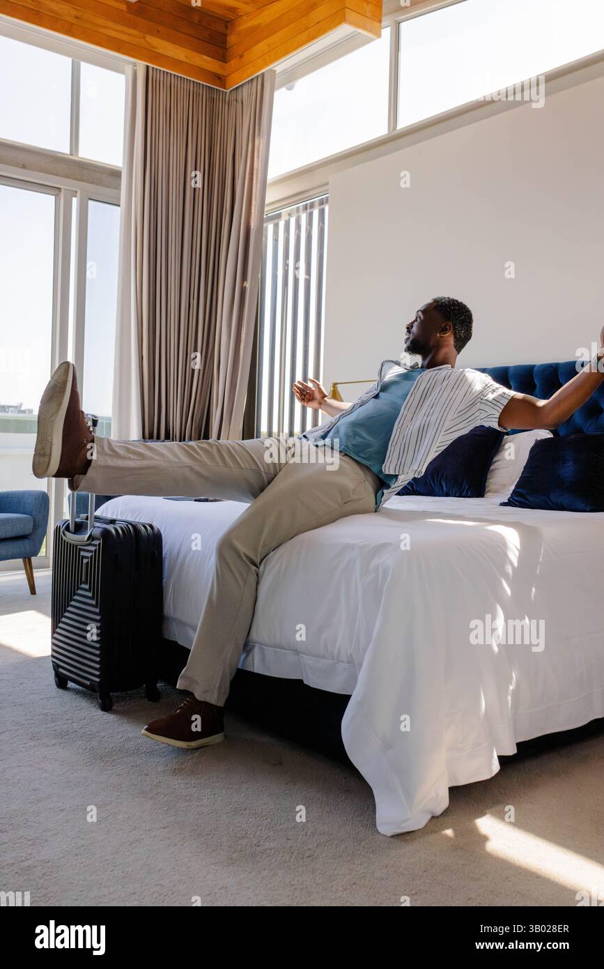 Relaxing African American man stretching legs on bed in hotel, with ...