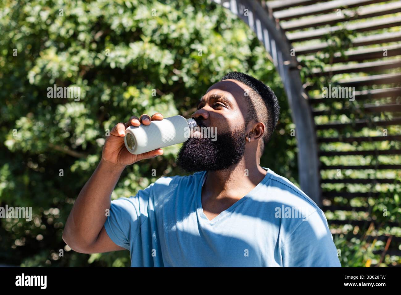 Drinking African American man tipping head back under garden pergola ...