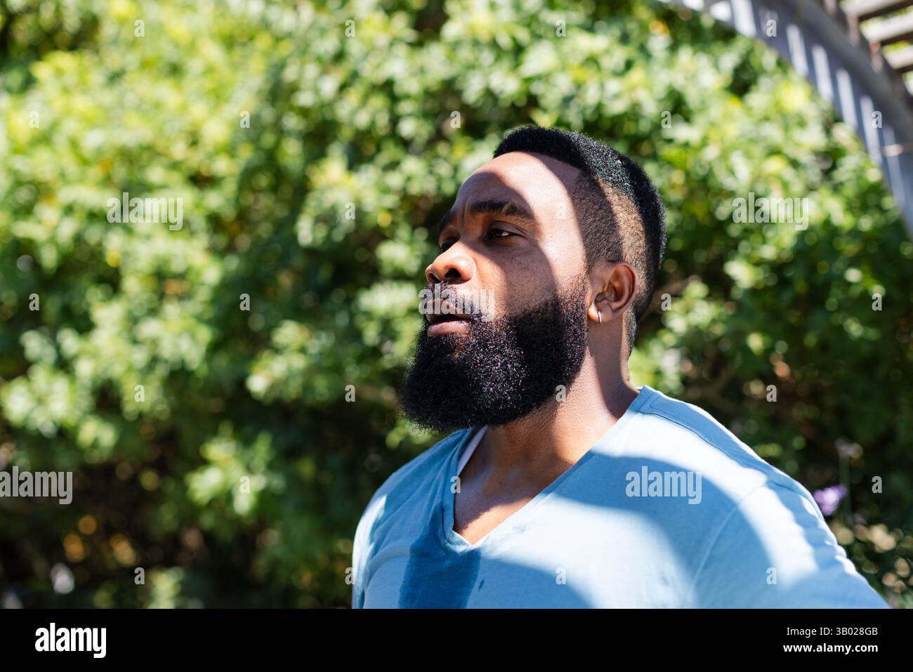Standing African American man gazing upward outdoors under slatted ...