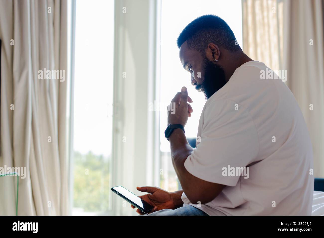 African American man holding smartphone and scrolling content by large window, copy space Stock ...