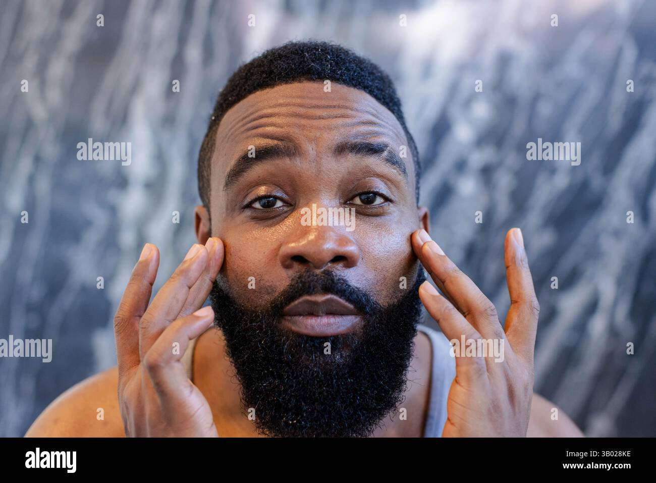 Touching cheeks mid adult African American man examining skin in ...
