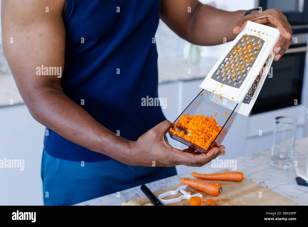 Grating African American man shredding carrots on kitchen countertop ...