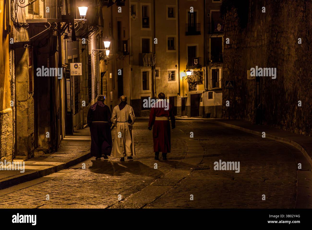 Three people in processional costumes walk through a Spanish alley at ...