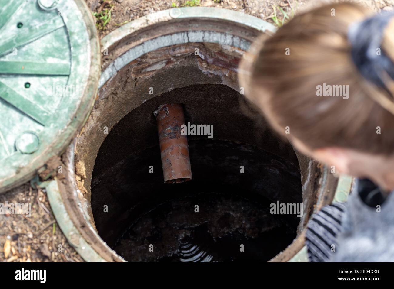 A woman looks into an open septic tank to check the level of sewer ...