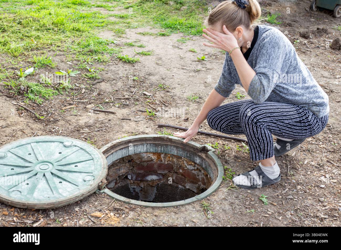 A woman looks into an open septic tank to check the level of sewer ...