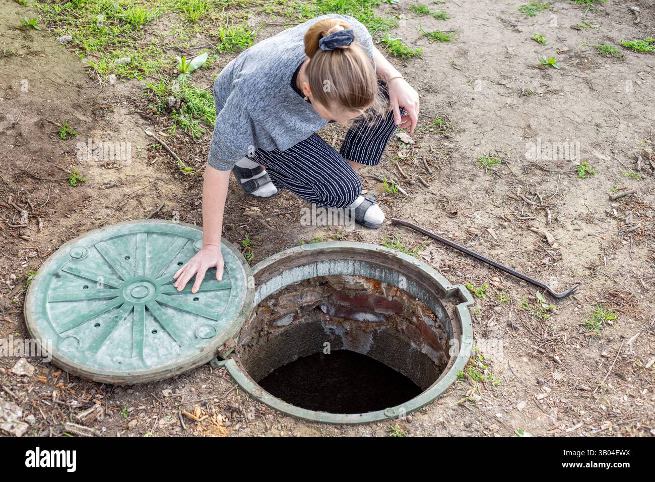 A woman looks into an open septic tank to check the level of sewer ...